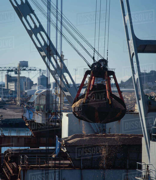 Close up of large claw bucket loading wood chips onto ship at port ...