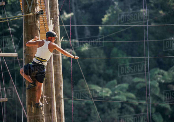 Man standing at top of poll ready to balance on suspended rope at ...
