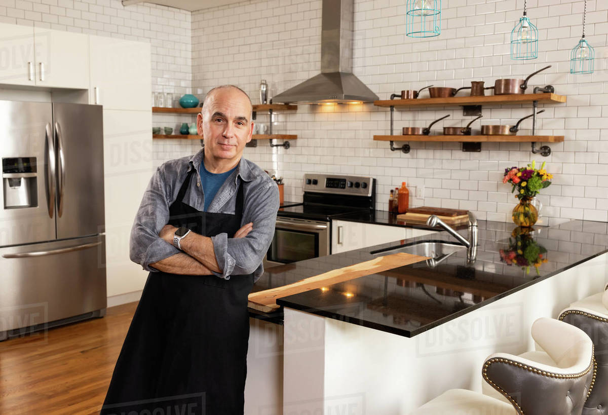 Man leaning against kitchen countertop with arms crossed looking into ...