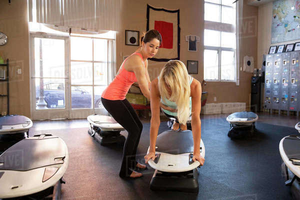 An instructor helping a woman exercise on a balance surfboard exercise ...