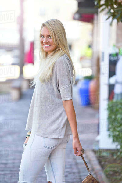 Woman looking back over her shoulder smiling while walking on city ...