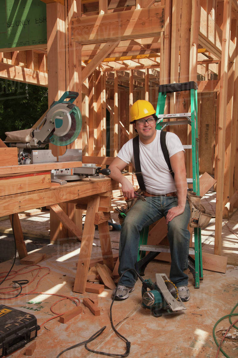 Man at a residential construction site sitting on a ladder and leaning ...
