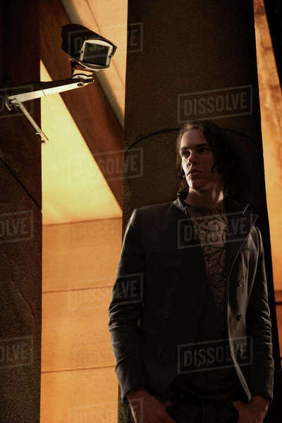 Young man standing outside building at night leaning on column with ...