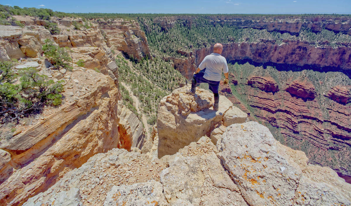 A man standing on a cliff overlooking the South Kaibab Trail east of ...