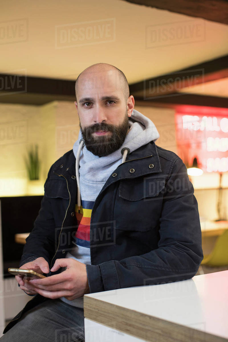 Man checking his phone while sitting at table in co-working space ...