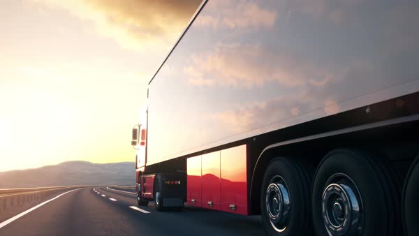 The camera follows a semi truck driving along a desert highway into the ...