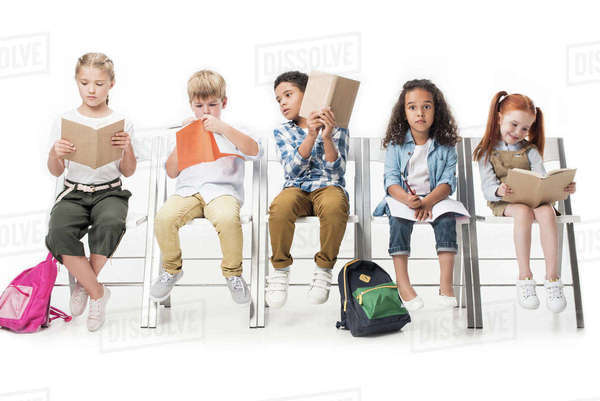 Multiethnic kids reading books while sitting on chairs isolated on ...