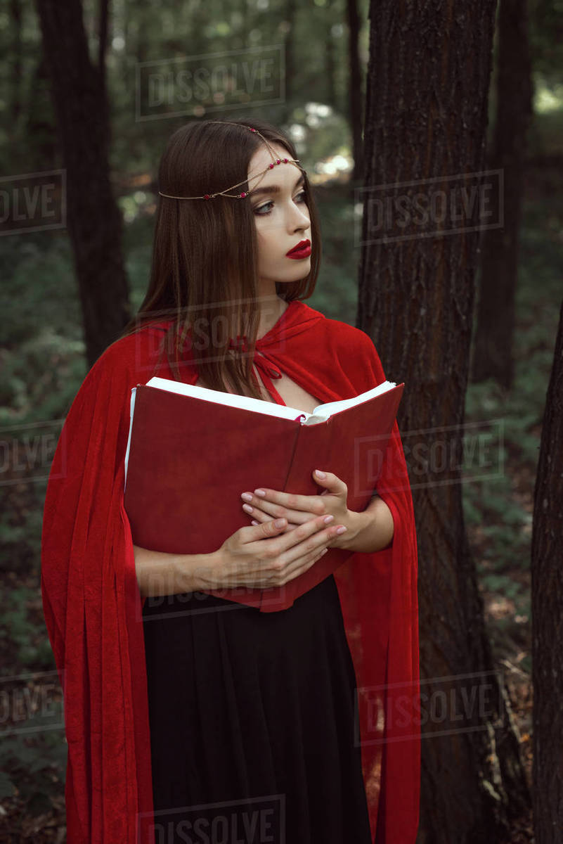 Beautiful mystic girl in red cloak and wreath holding magic book in ...