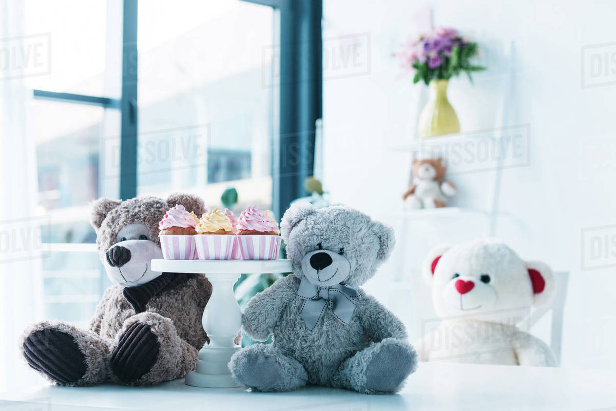 Selective focus of teddy bears on table with cupcakes on stand ...
