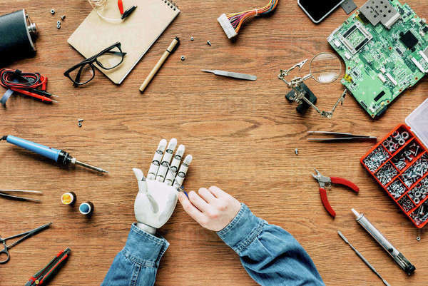 Cropped image of man fixing robotic hand by screwdriver at wooden table ...