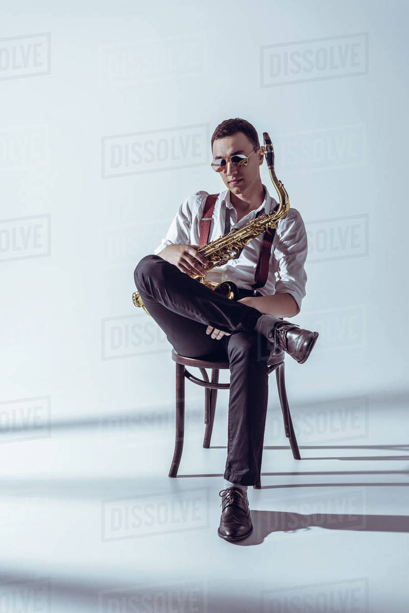Stylish young performer in sunglasses sitting on chair and holding ...