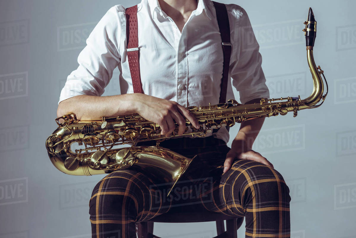 Cropped shot of young musician sitting on chair and holding saxophone ...