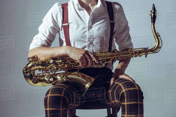 Cropped shot of young musician sitting on chair and holding saxophone ...