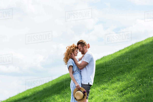 Side view of happy redhead couple standing face to face on green hill ...
