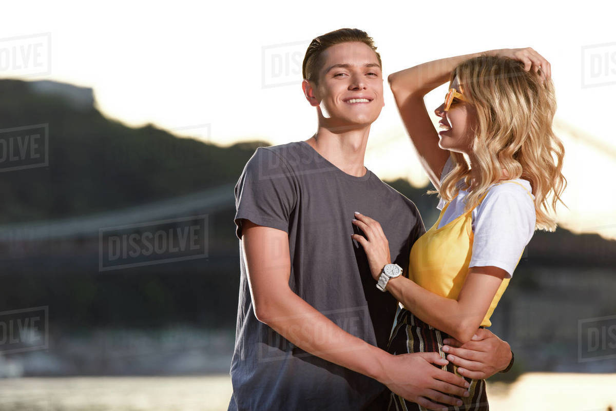 boyfriend hugging girlfriend on river beach in evening and looking at ...