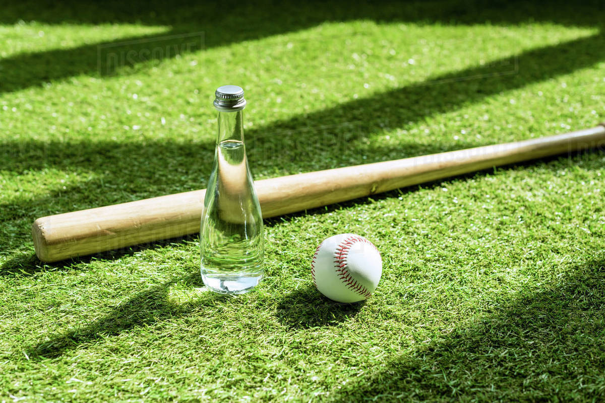 glass water battle with baseball ball and bat lying on green grass ...
