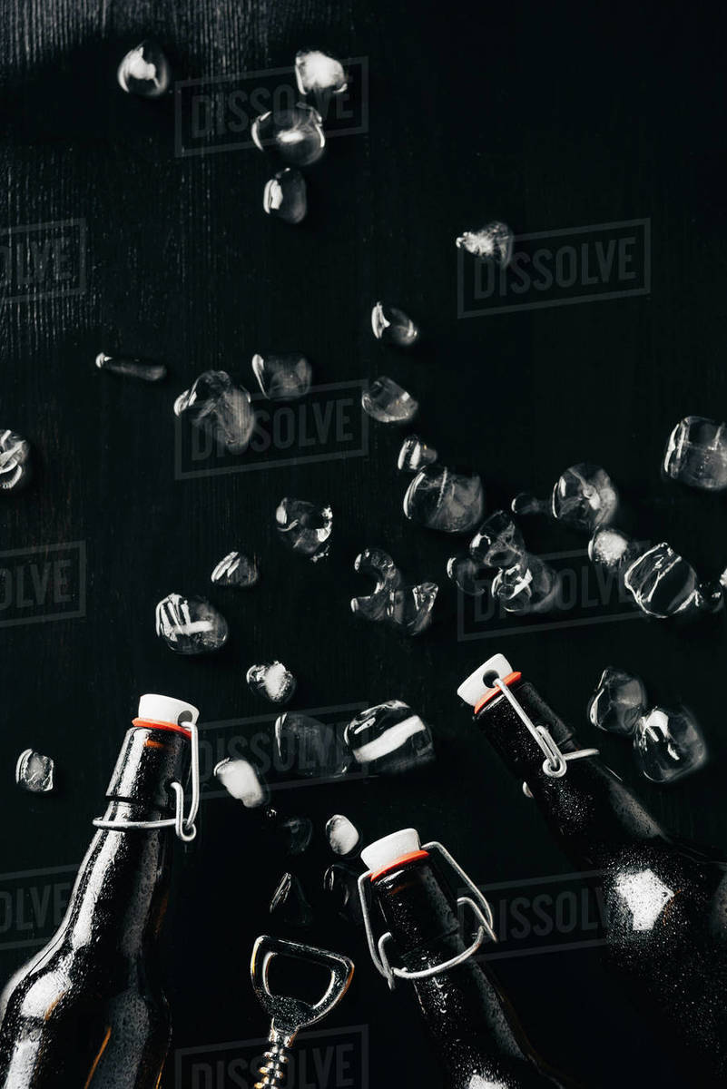 flat lay with bottle opener, glass bottles of beer and ice cubes ...