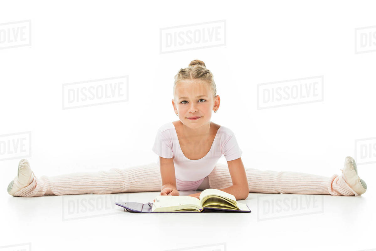 Smiling little ballerina reading book and doing twine isolated on white ...