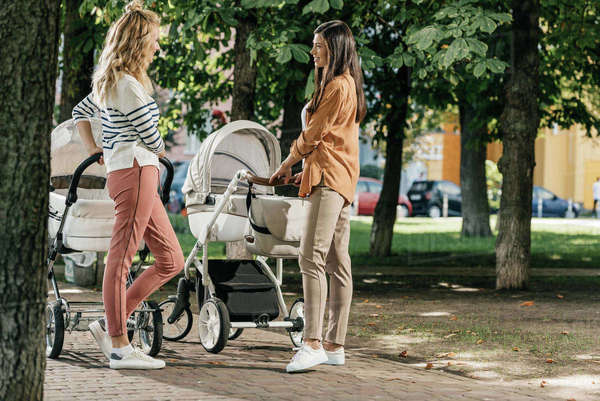 Side view of mothers talking and standing with baby strollers in park ...