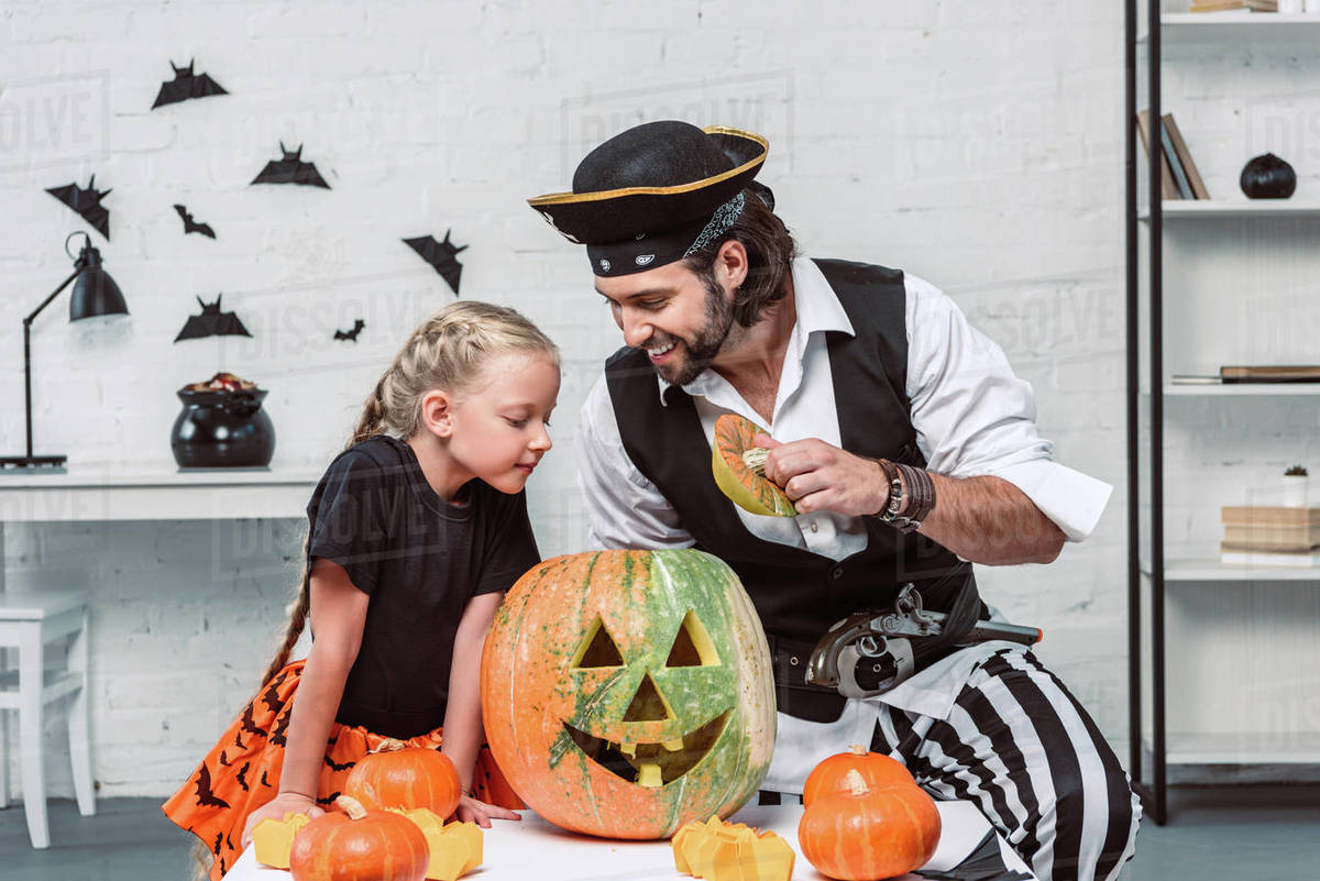 Father and daughter in halloween costumes looking into pumpkin together ...