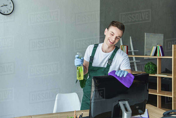Happy young professional cleaner holding rag with detergent and ...