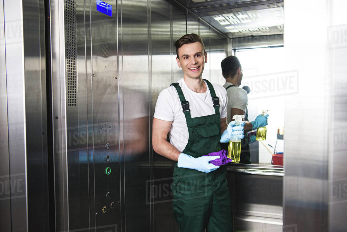 Handsome young janitor holding spray bottle with detergent and rag ...