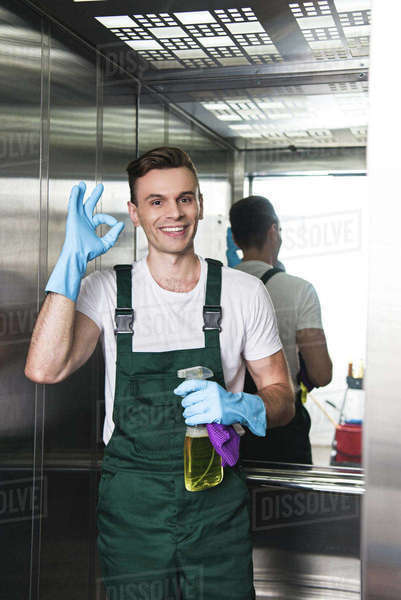 Handsome young janitor holding spray bottle with detergent and rag ...