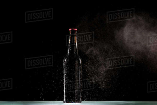 Beer bottle with spraying water around at surface on black background ...