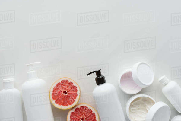 Flat lay with containers of lotion and pieces of grapefruit on white ...
