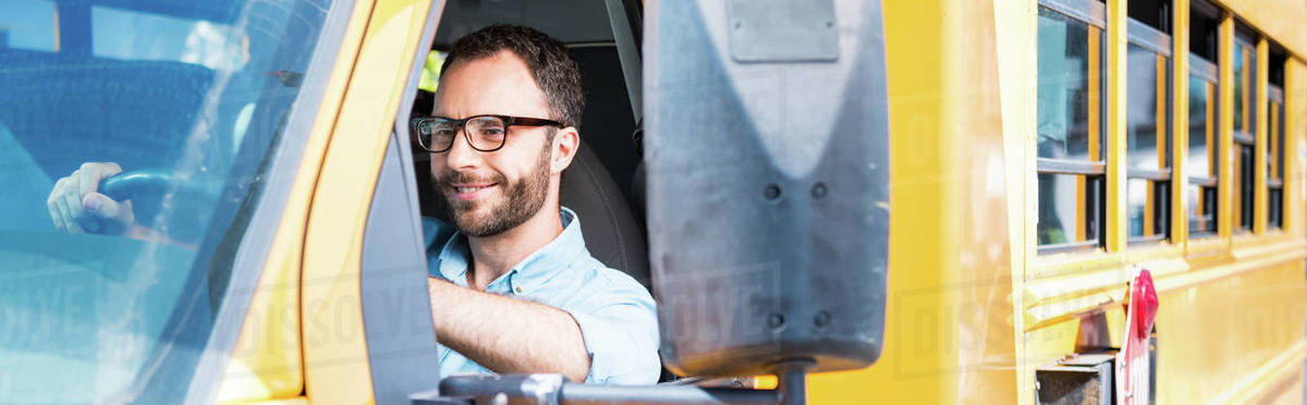 panoramic shot of handsome school bus driver smiling and driving ...