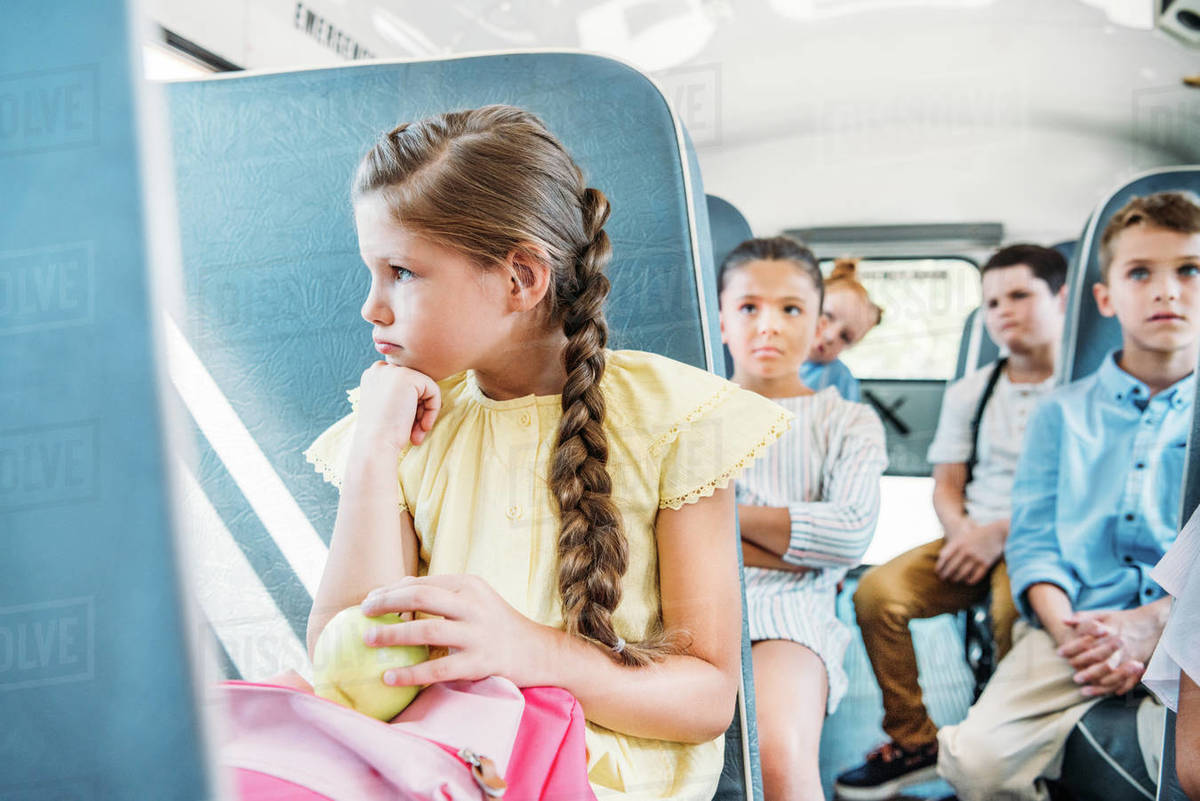 sad little schoolgirl riding on school bus with her classmates ...