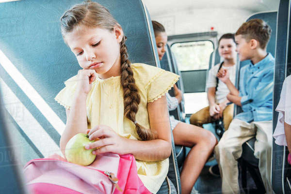 sad little schoolgirl riding on school bus while her classmates ...