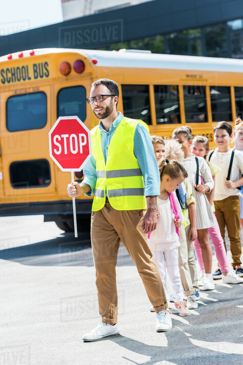 traffic guard crossing road with happy pupils in front of school bus ...