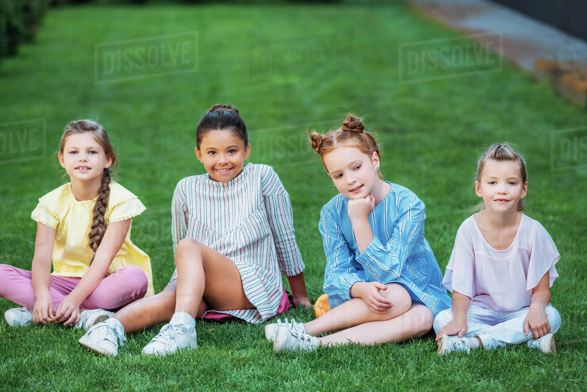 group of adorable schoolgirls sitting on green grass together and ...