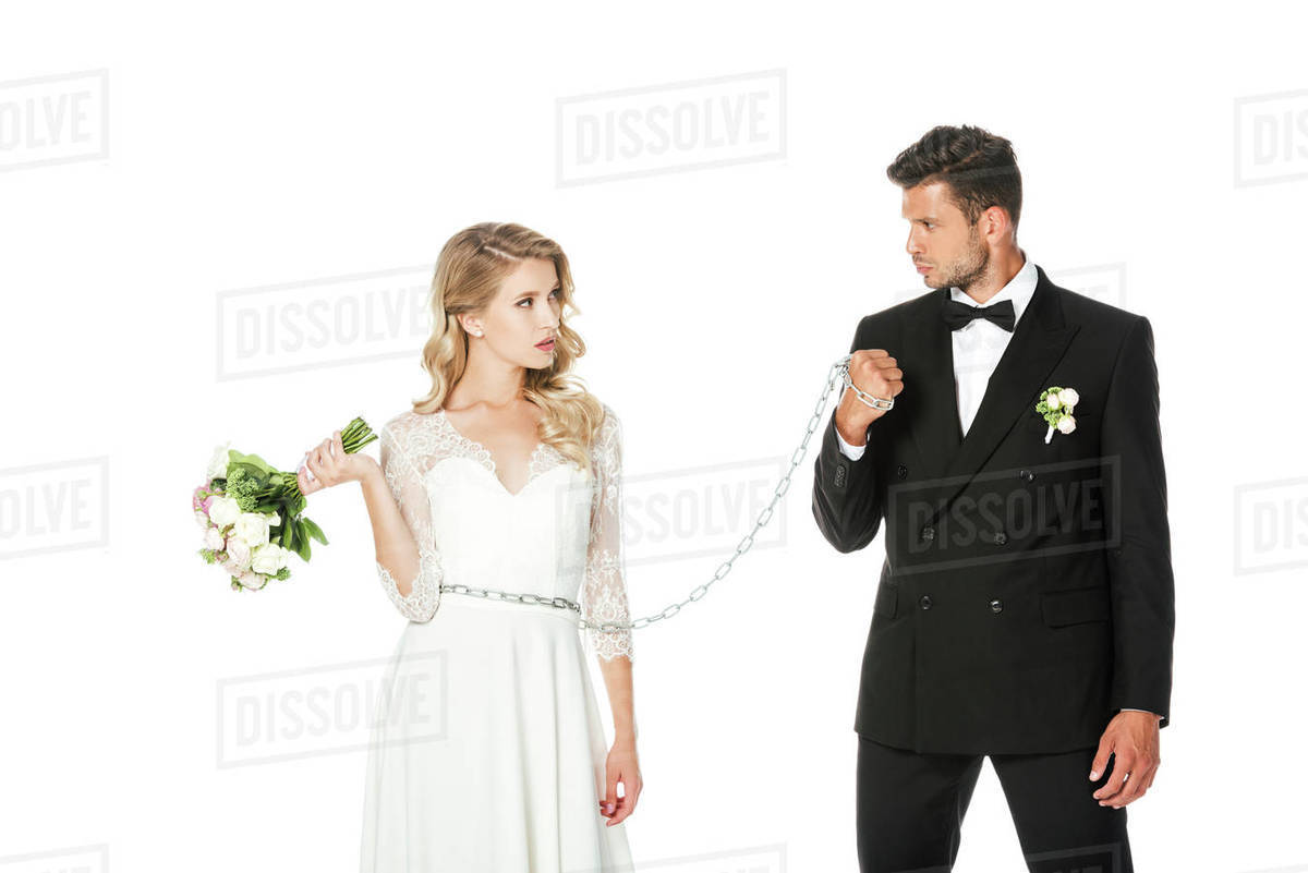 Young groom with chain and leashed bride looking at each other isolated ...