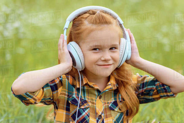 portrait of smiling kid listening music in headphones with green grass ...