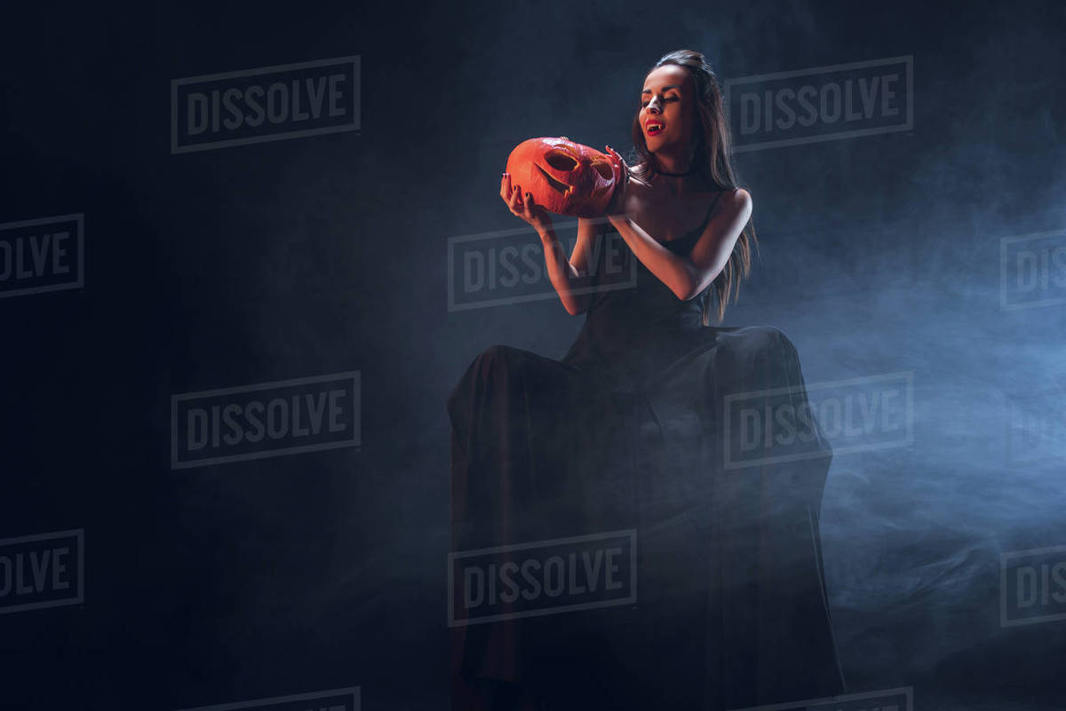 Beautiful woman in vampire costume holding jack o lantern on dark ...