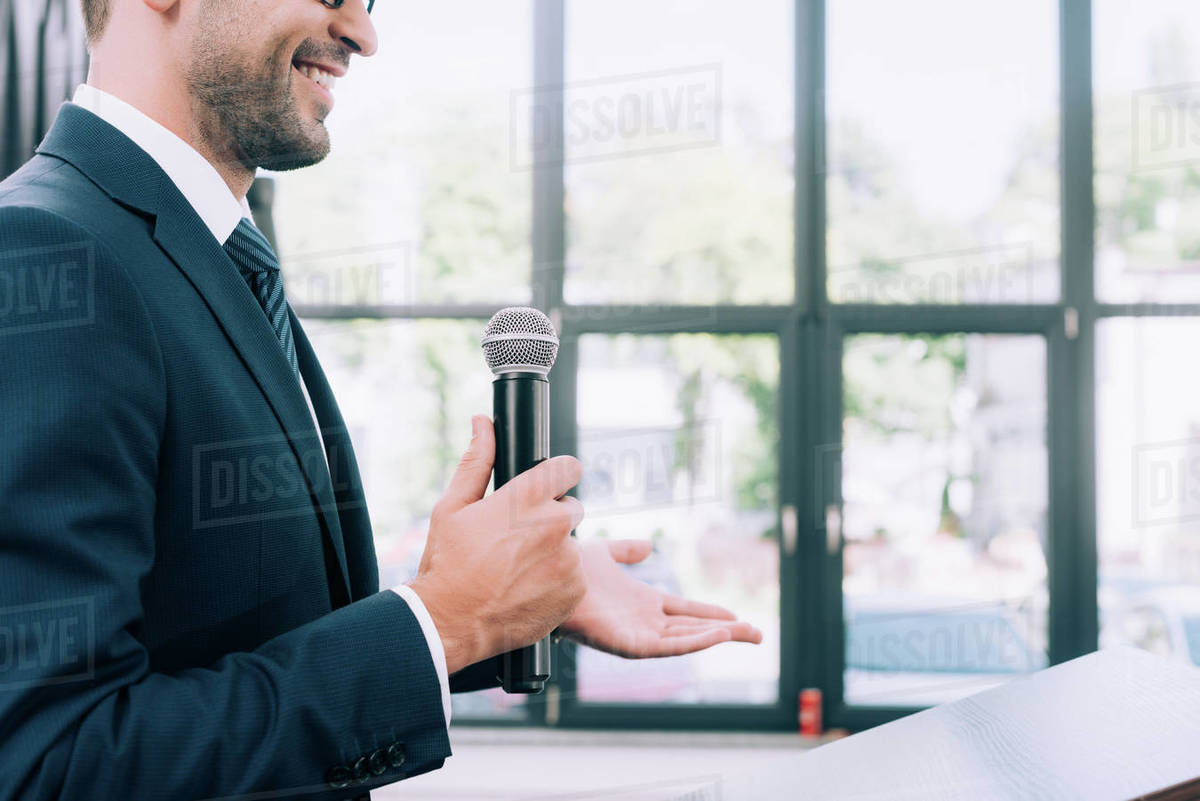 Cropped image of smiling speaker gesturing and talking into microphone ...