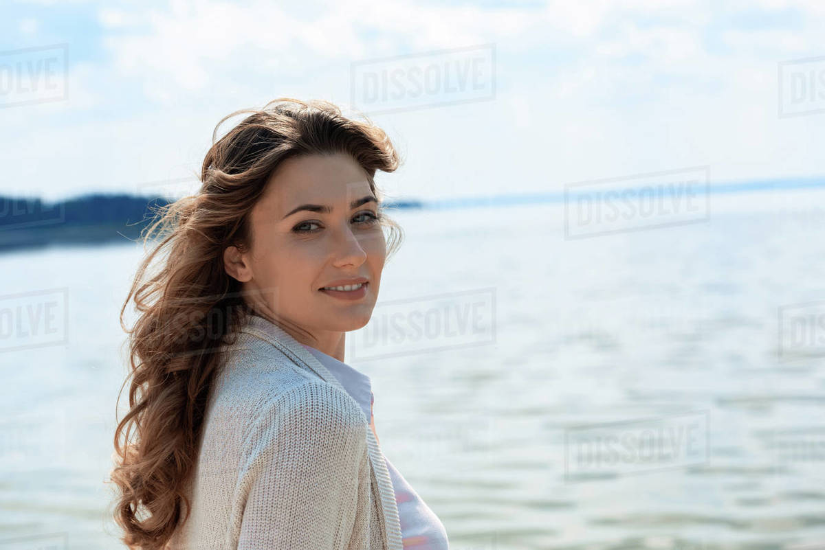 Side view of beautiful woman looking at camera with river on background ...