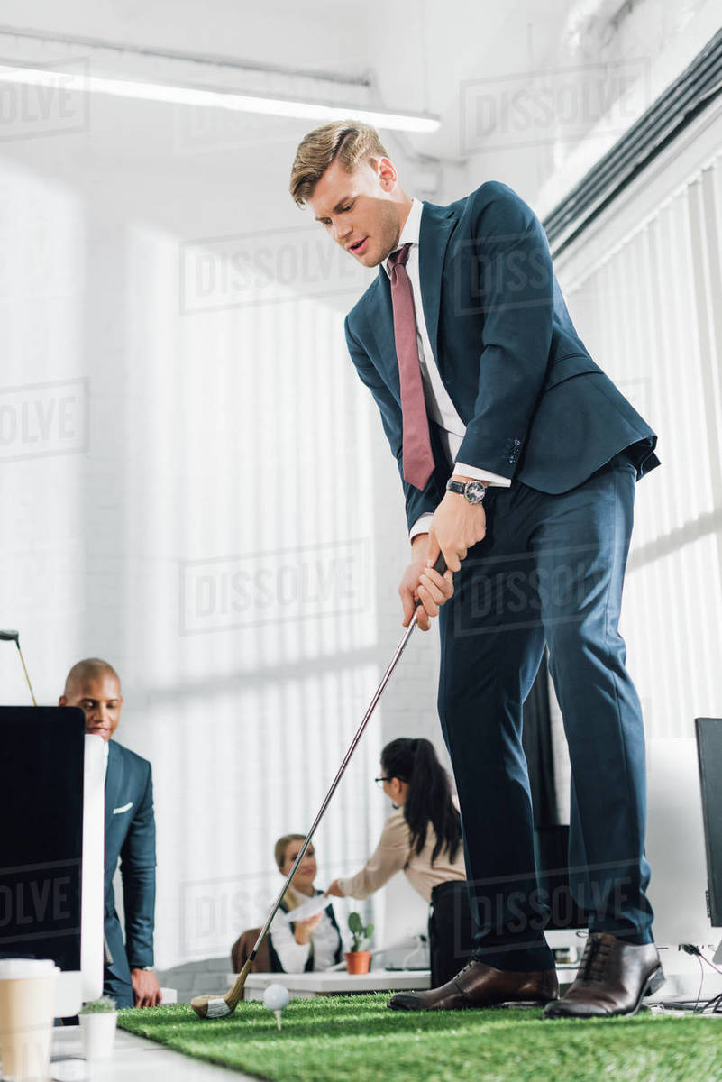 Low angle view of young businessman playing golf in office - Royalty ...