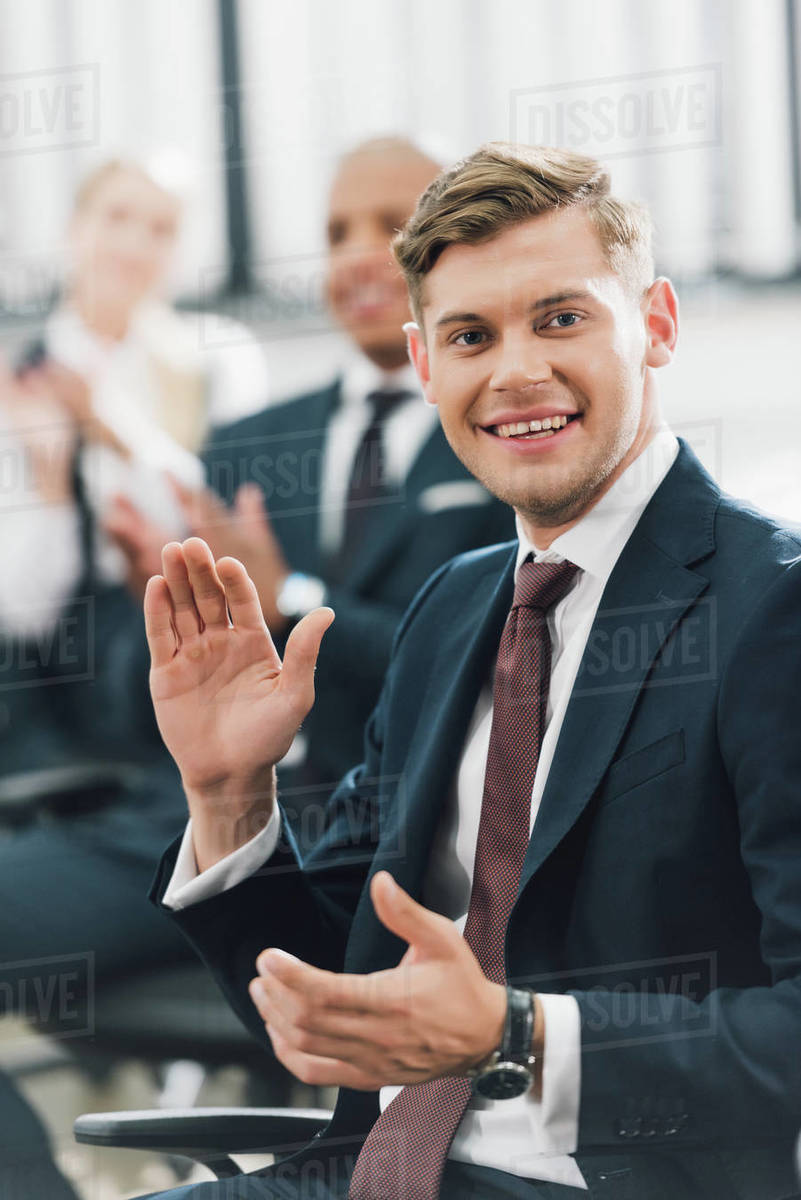 Happy young businessman waving hand and smiling at camera in office ...