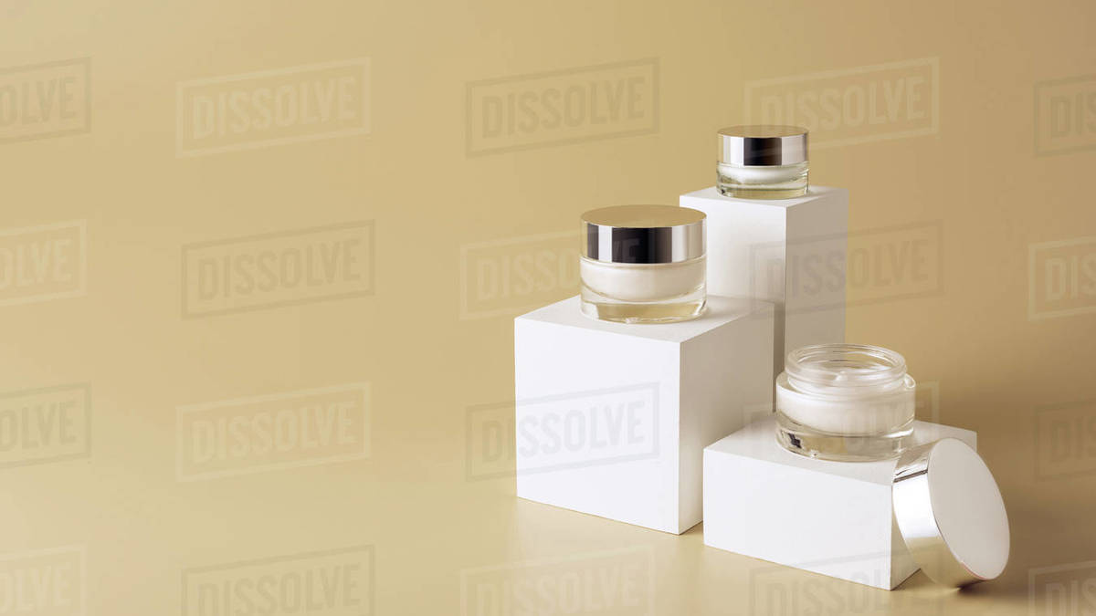 close up view of facial and body creams in glass jars on white cubes on ...