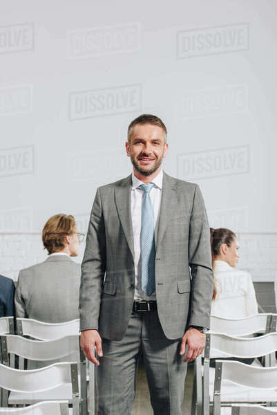 smiling handsome coach looking at camera during business training in ...