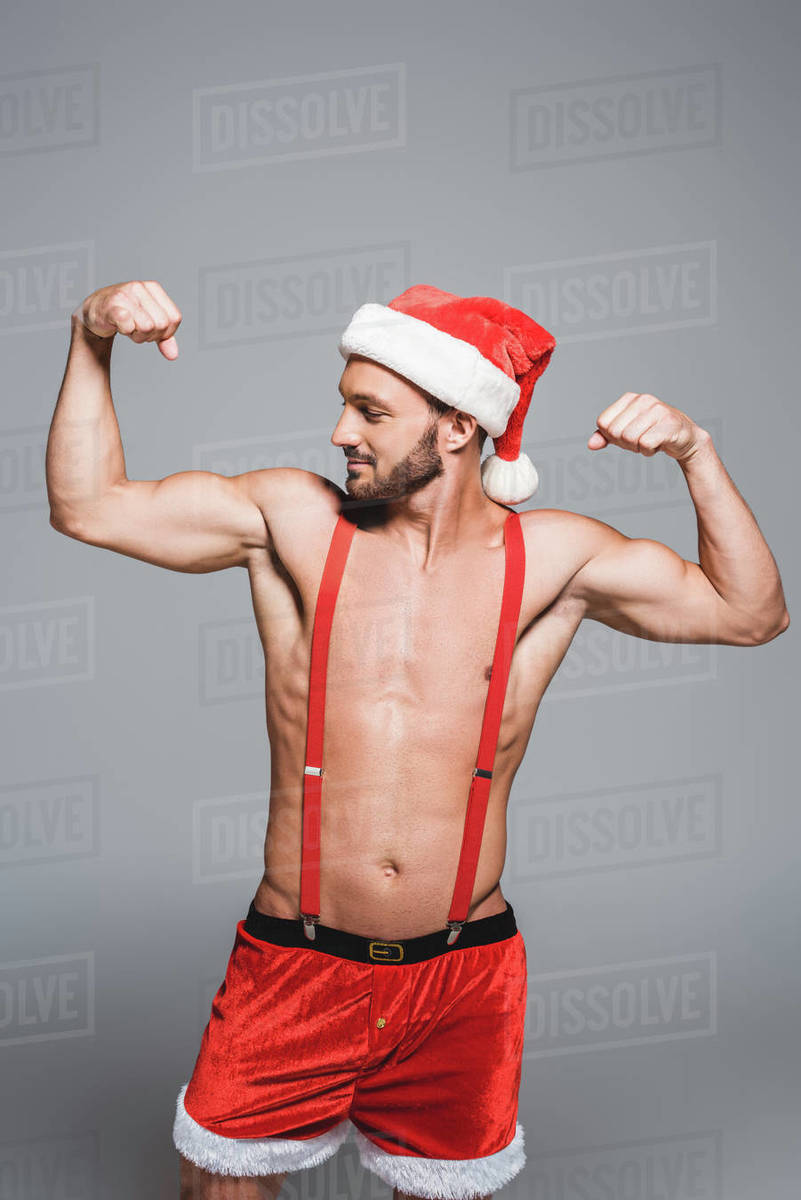 Sexy muscular man in christmas hat showing muscles isolated on grey ...