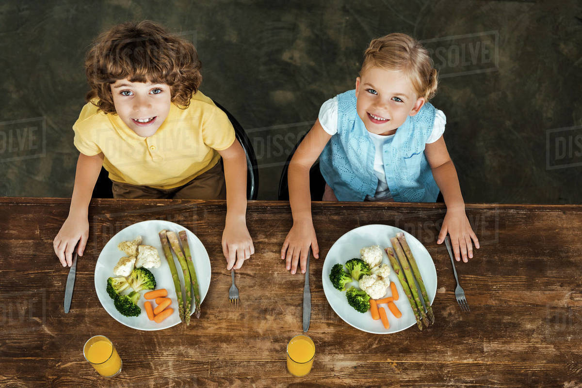 High angle view of adorable happy kids eating healthy vegetables and ...