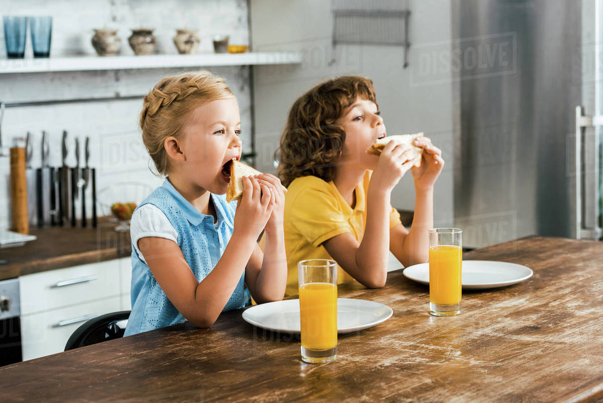 Beautiful children sitting at table and eating tasty sandwiches ...