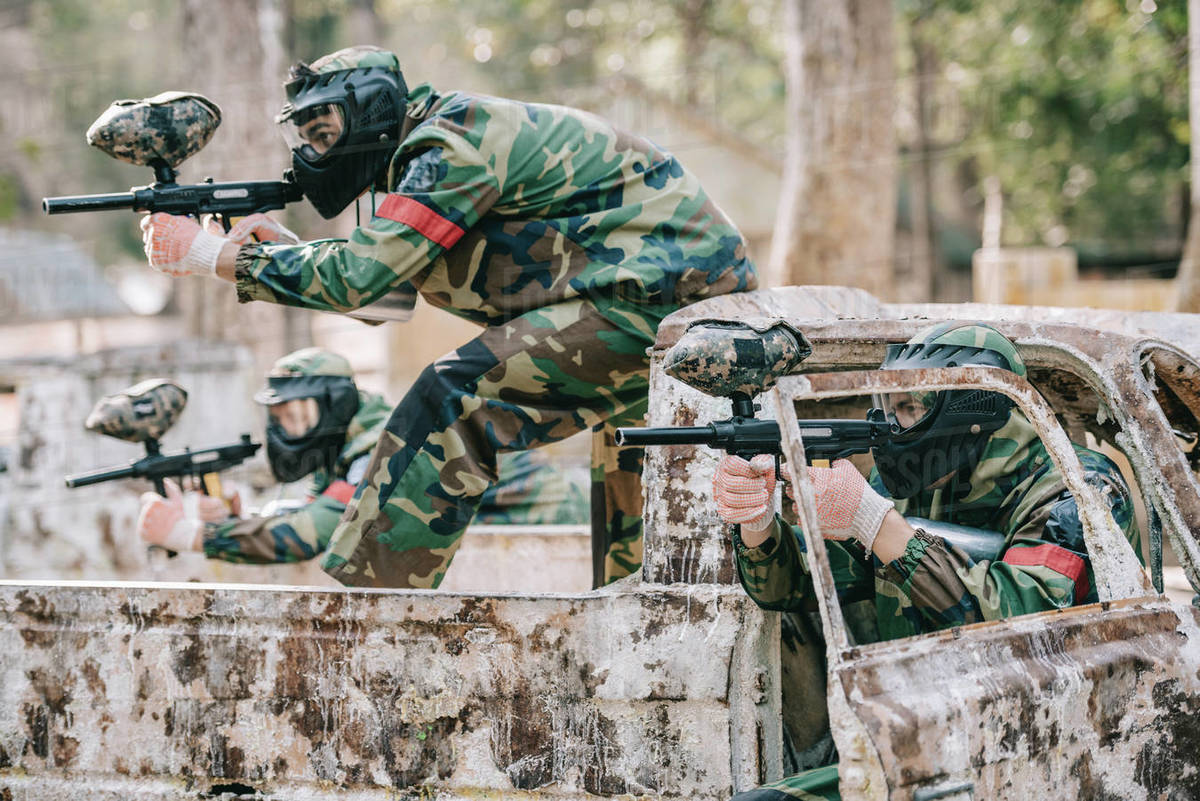 Paintball team in protective masks and camouflage aiming by marker guns ...