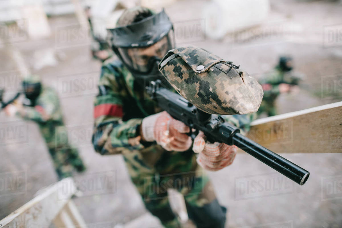 Selective focus of male paintball player aiming by marker gun on ...