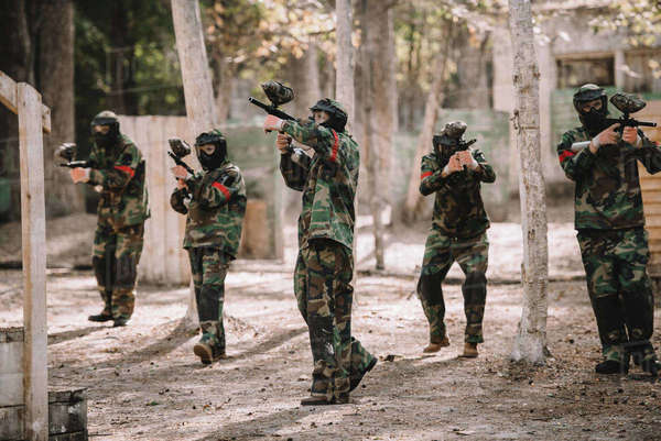 Paintball team in uniform and protective masks shooting by paintball ...
