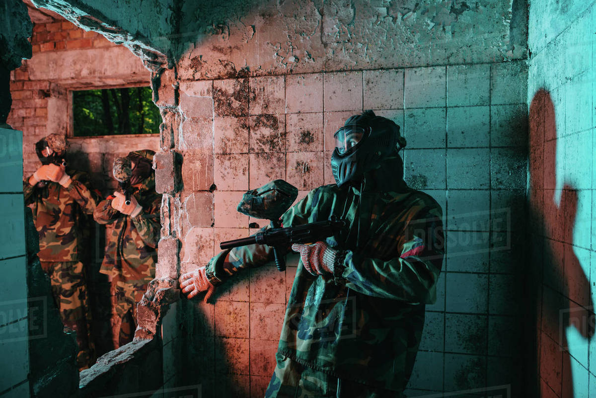 Male paintball player in goggle mask and camouflage uniform hiding ...